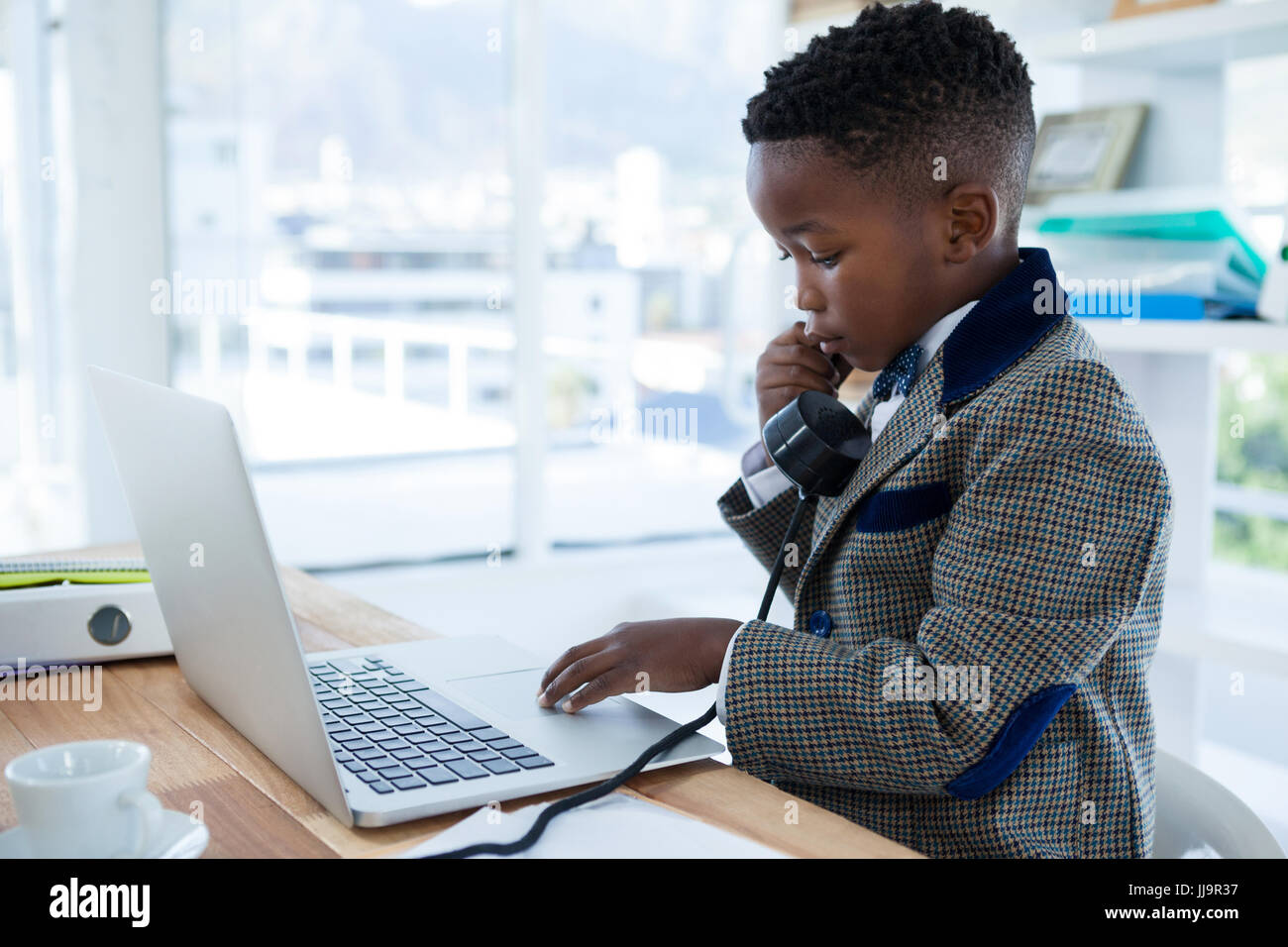 Businessman scrolling on laptop while using telephone at table in ...