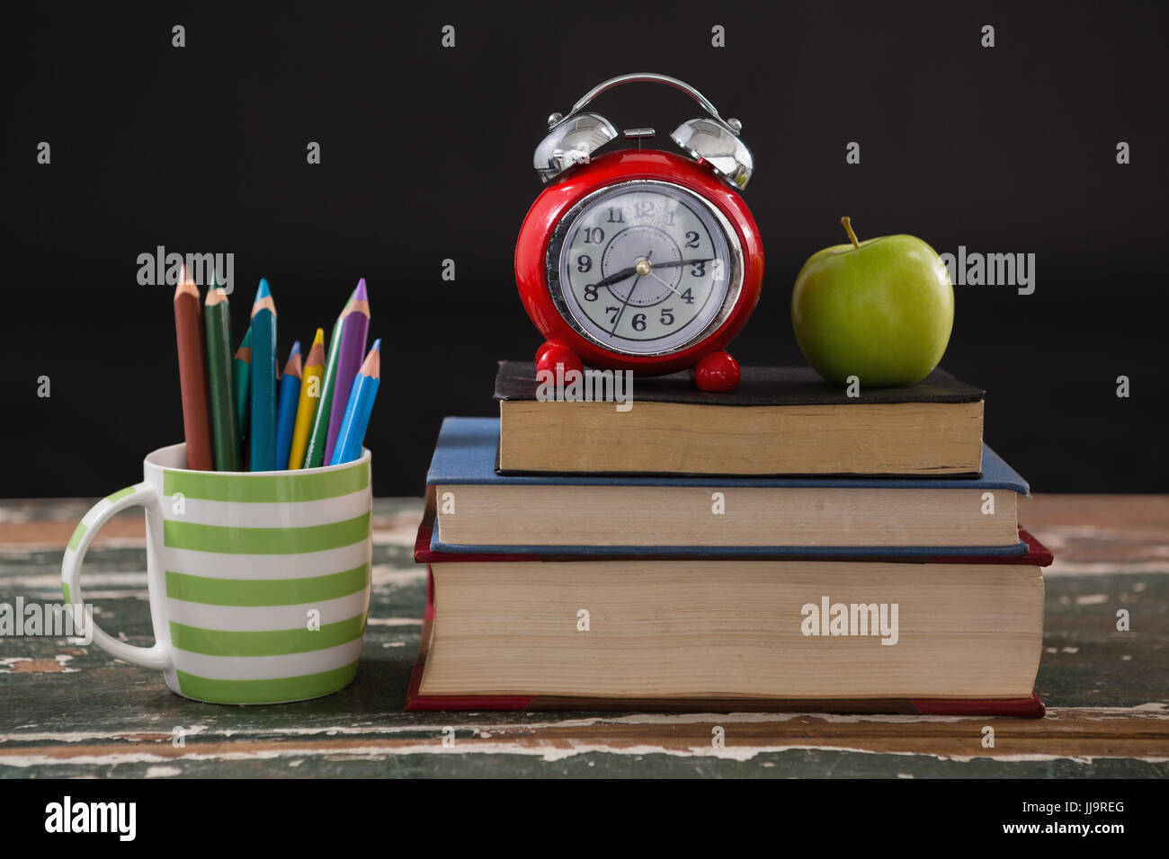 Close-up of alarm clock and apple on stack of books with pen holder ...