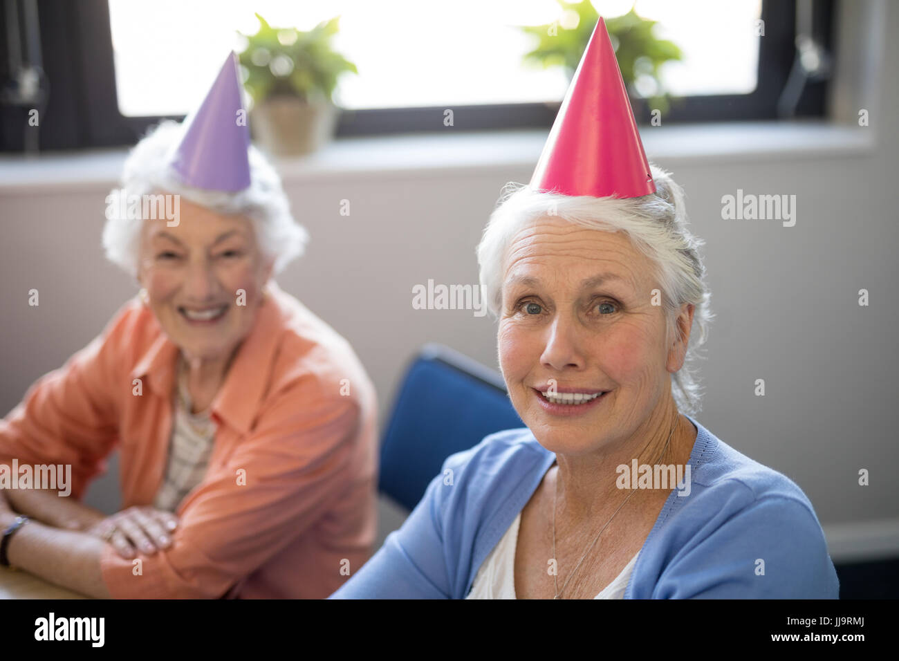 Portrait of smiling senior friends wearing party hats at nursing home ...