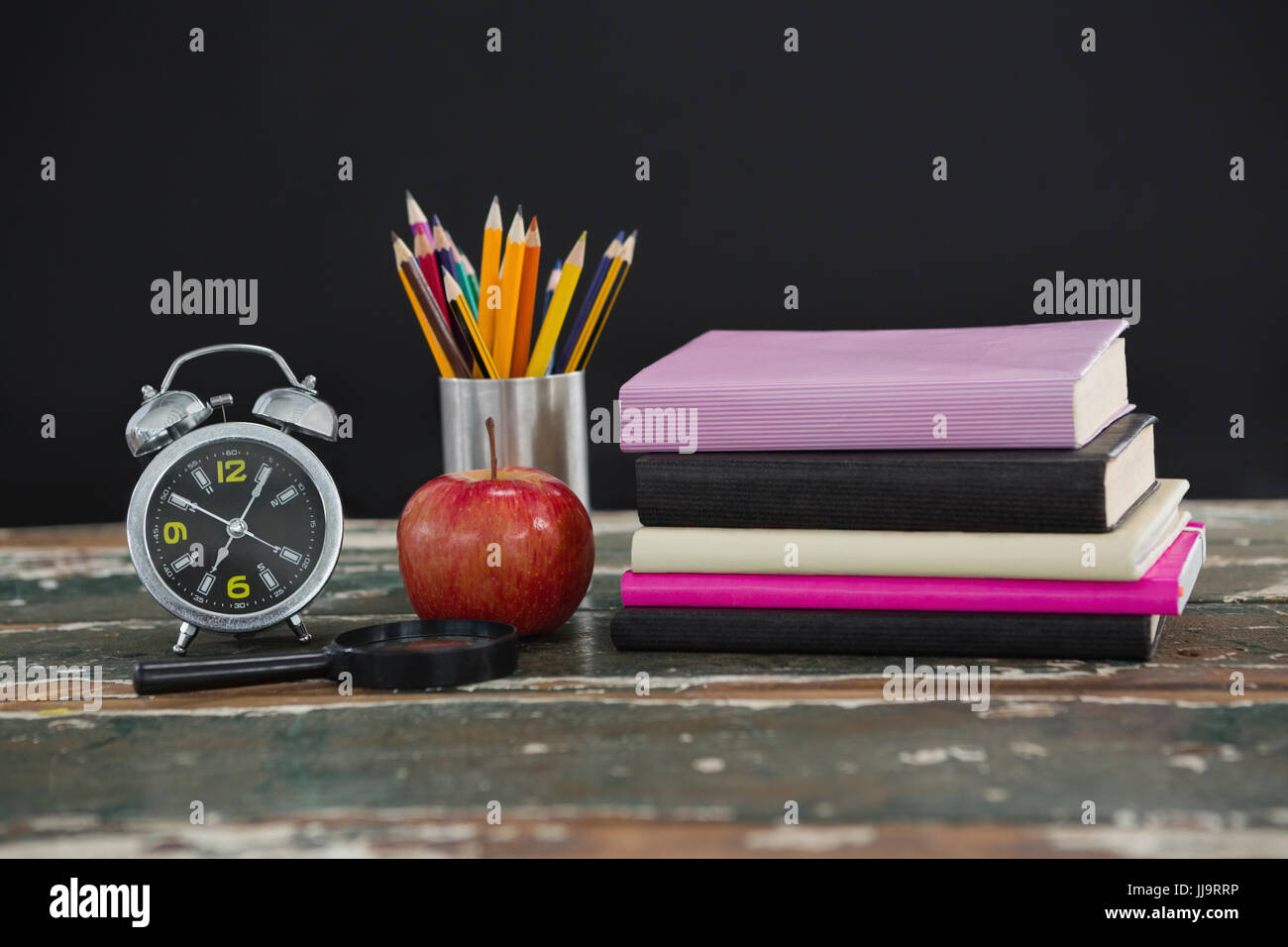 Stack of books with alarm clock, magnifying glass, apple and pen holder ...