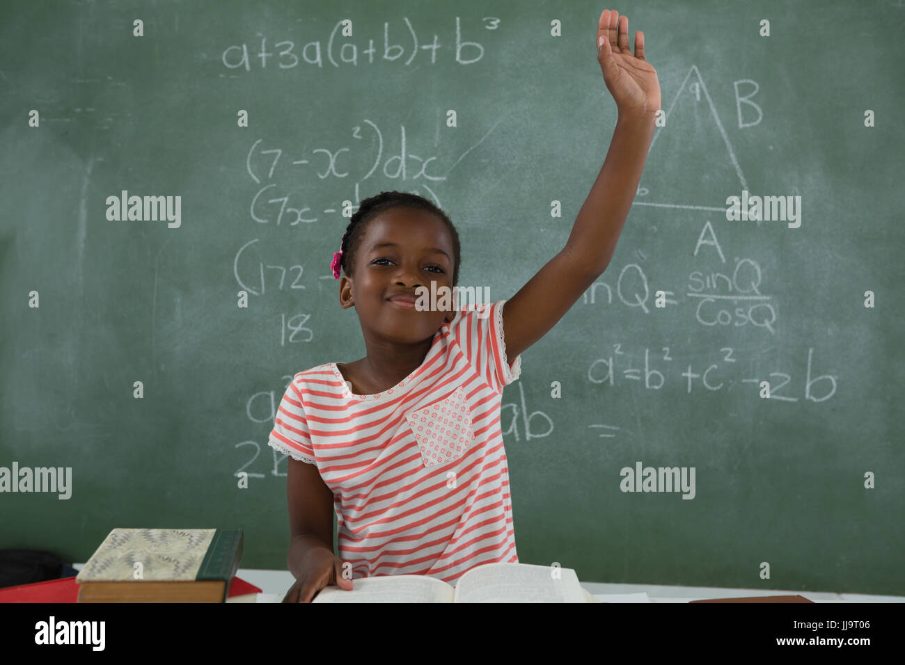 Portrait of schoolgirl raising hand while sitting in classroom Stock ...