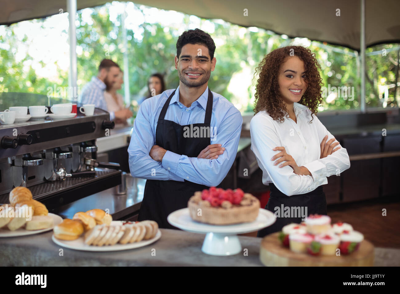 Portrait of smiling waiter and waitress standing with arms crossed at ...