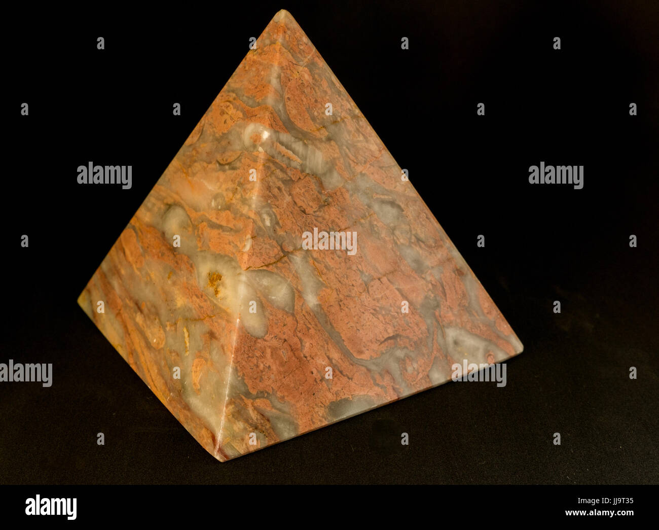 Still life of peach coloured marble pyramid against a black background ...