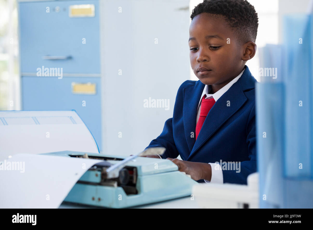 Boy imitating as businessman using typewriter while working at desk in ...