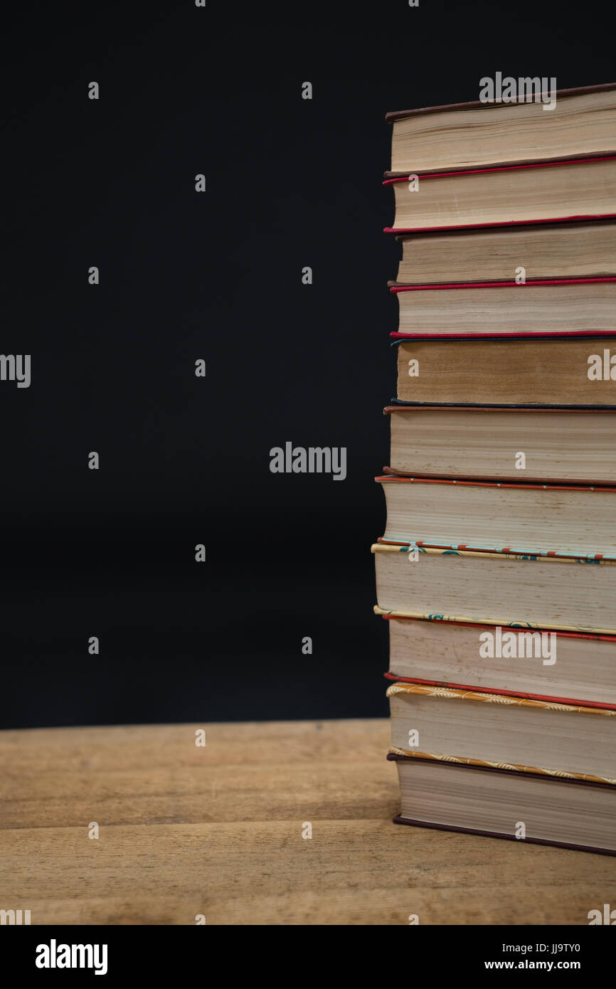Stacked books on wooden table against black background Stock Photo - Alamy
