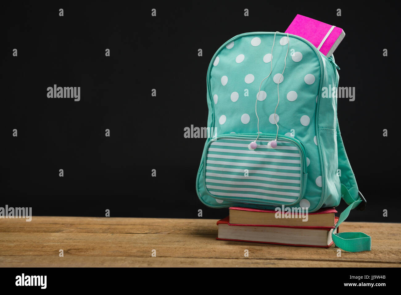 Schoolbag on book stack against black background Stock Photo - Alamy