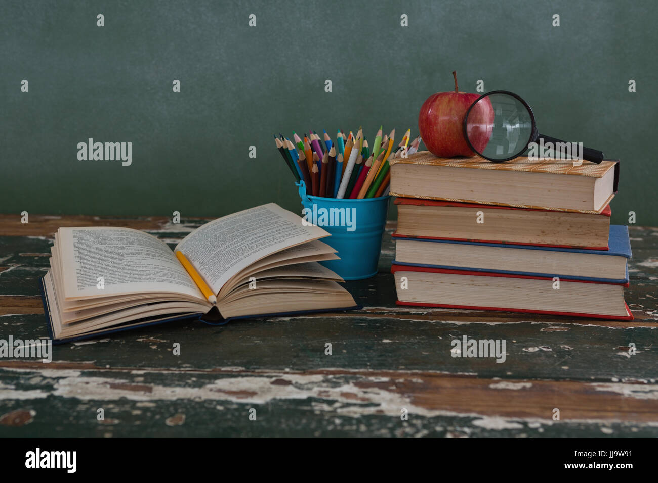 Stack of books with magnifying glass, apple and pen holder on wooden ...