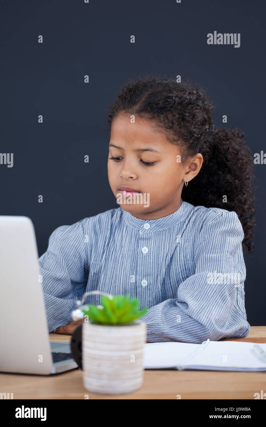 Businesswoman using laptop while sitting at desk against black ...