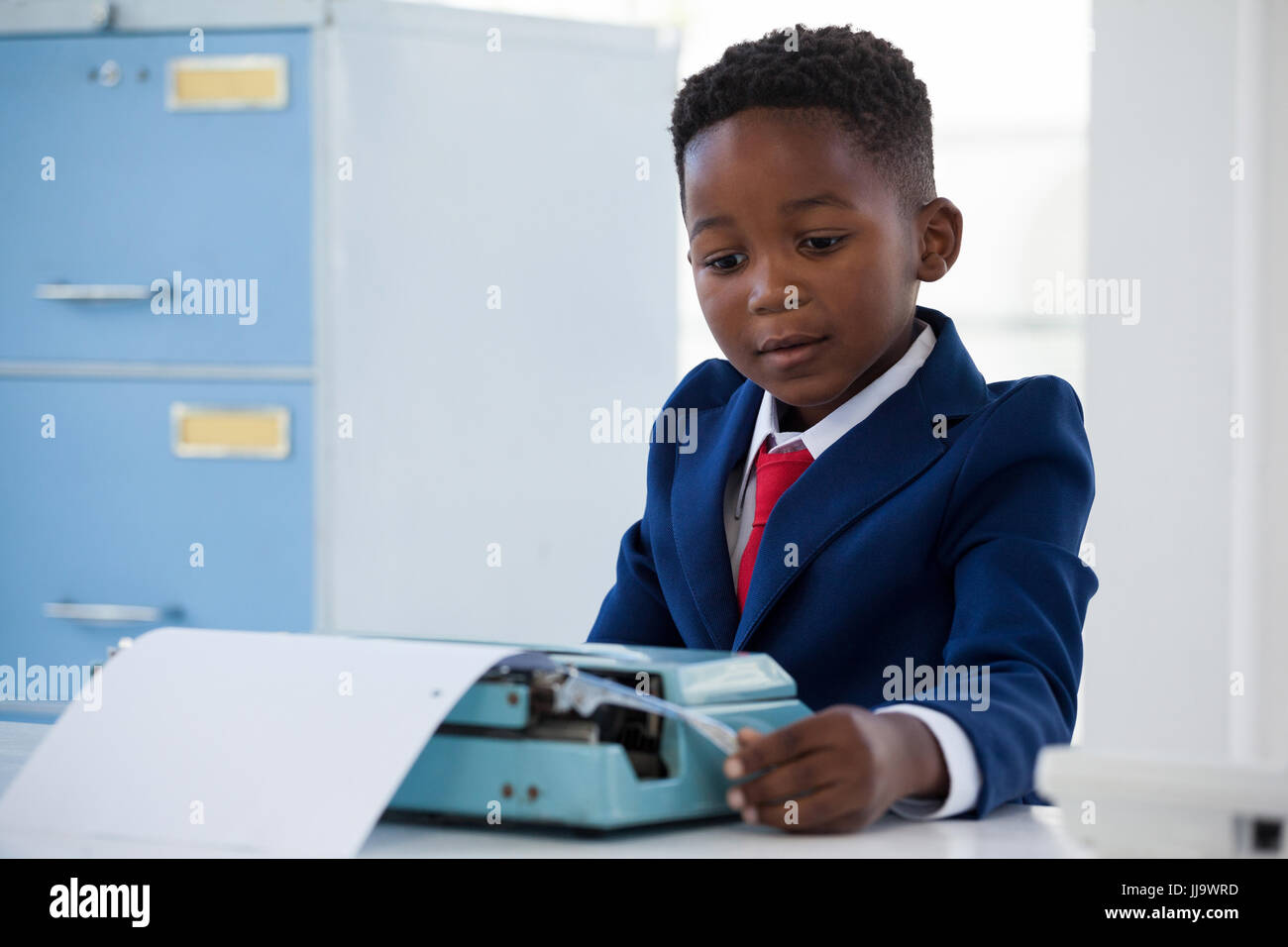 Boy imitating as businessman working on typewriter at desk in office ...