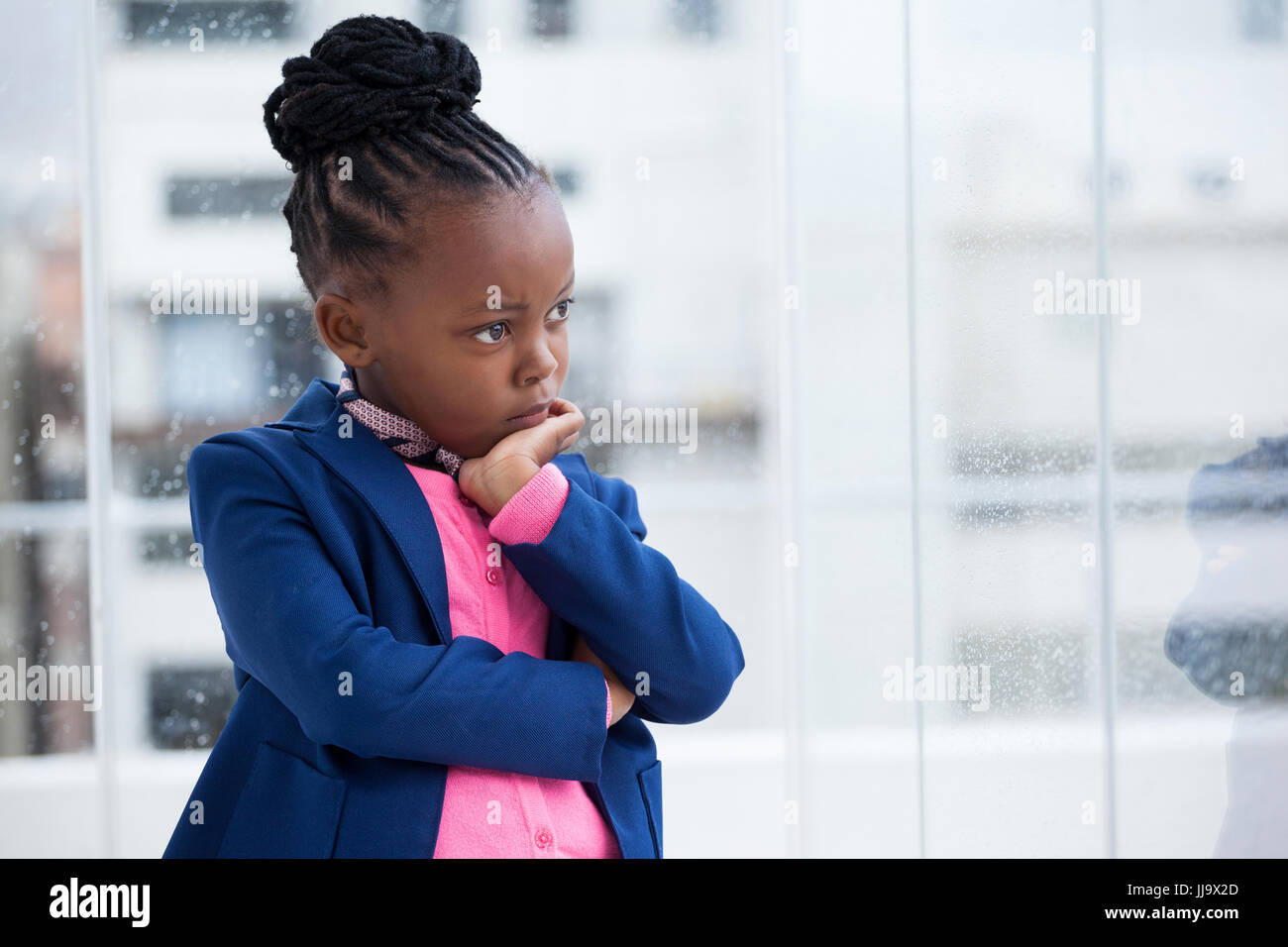 Thoughtful businesswoman with hand on chin standing by glass window at ...