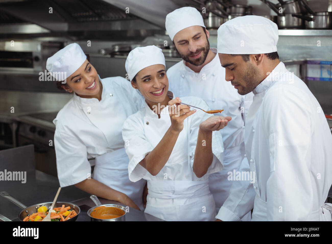 Chef tasting food to colleague in kitchen at restaurant Stock Photo - Alamy