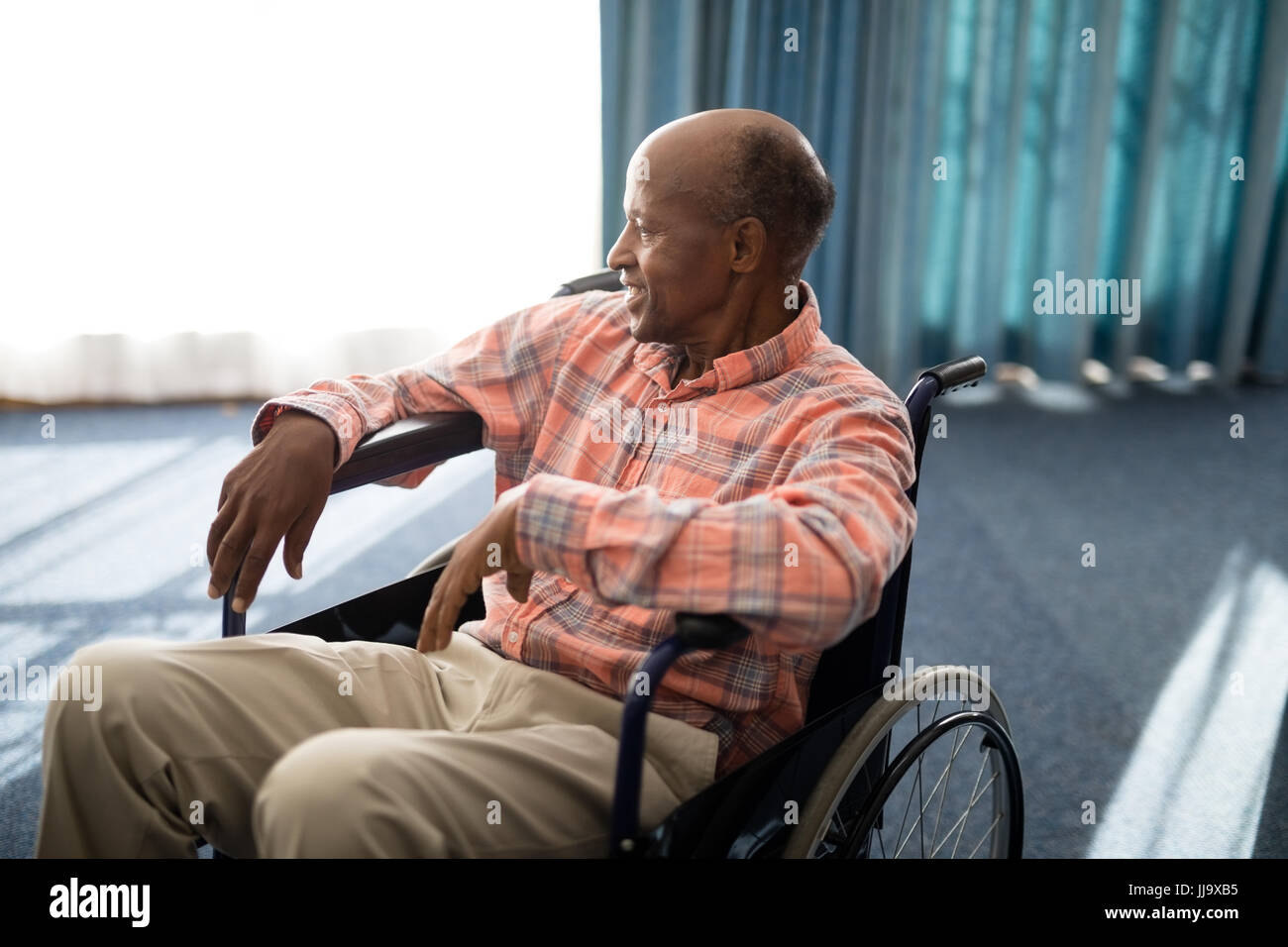 Smiling disabled senior man sitting on wheelchair against window at ...