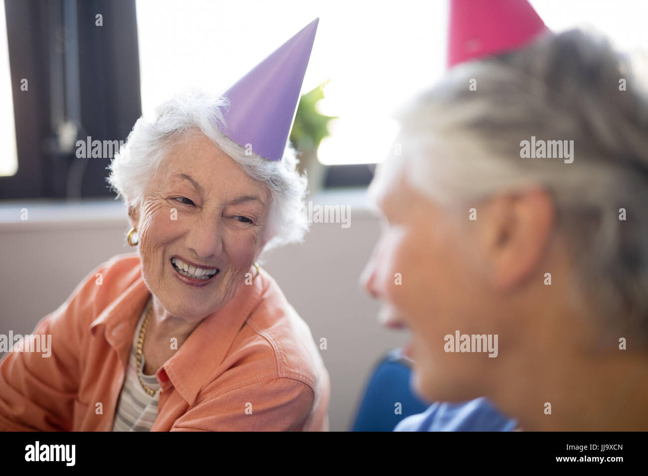 Smiling senior women wearing party hats talking at nursing home Stock ...