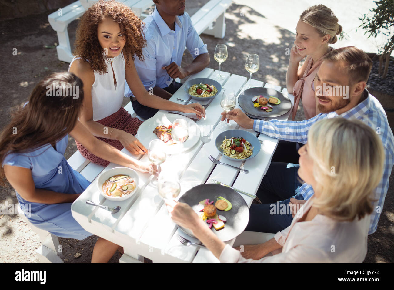 Happy friends interacting with each other while having meal in ...