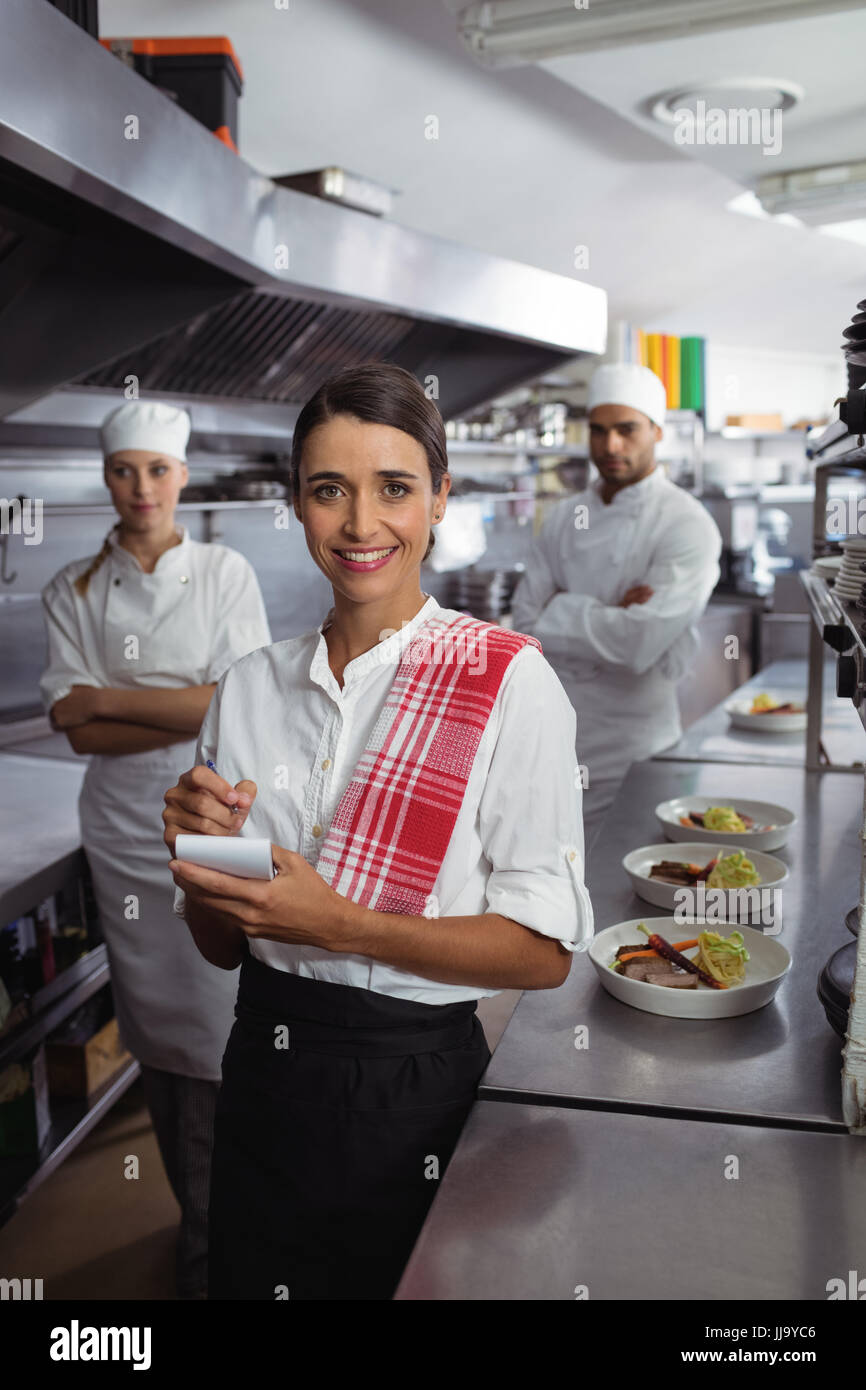 Portrait of waitress standing with kitchen staff in commercial kitchen ...