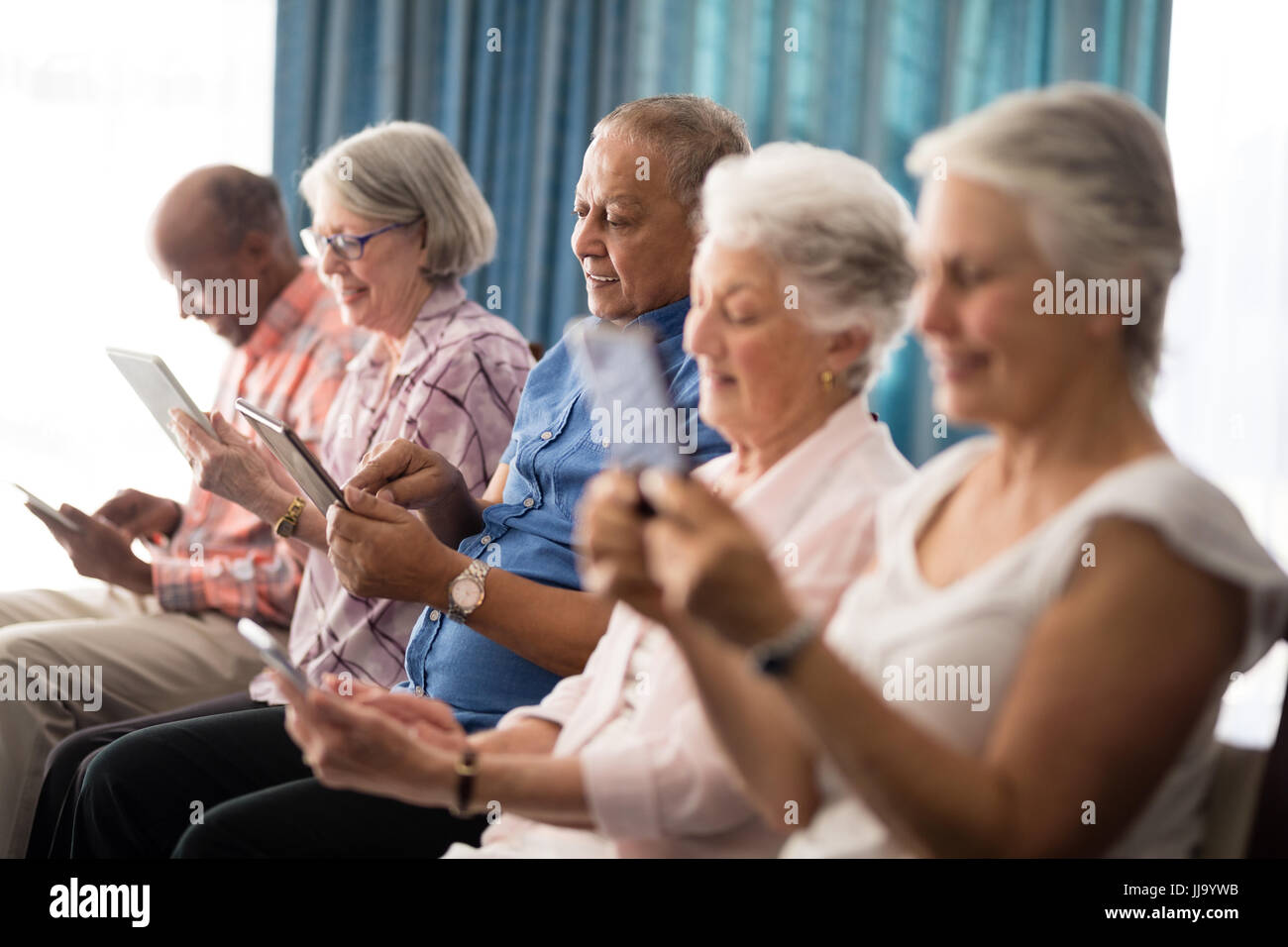Smiling senior people using digital tablets while sitting on chairs at ...