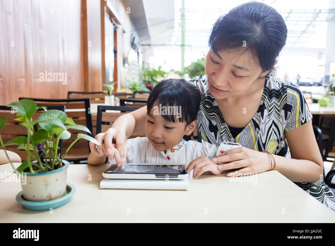 Asian Chinese little girl playing tablet computer with her mother at ...