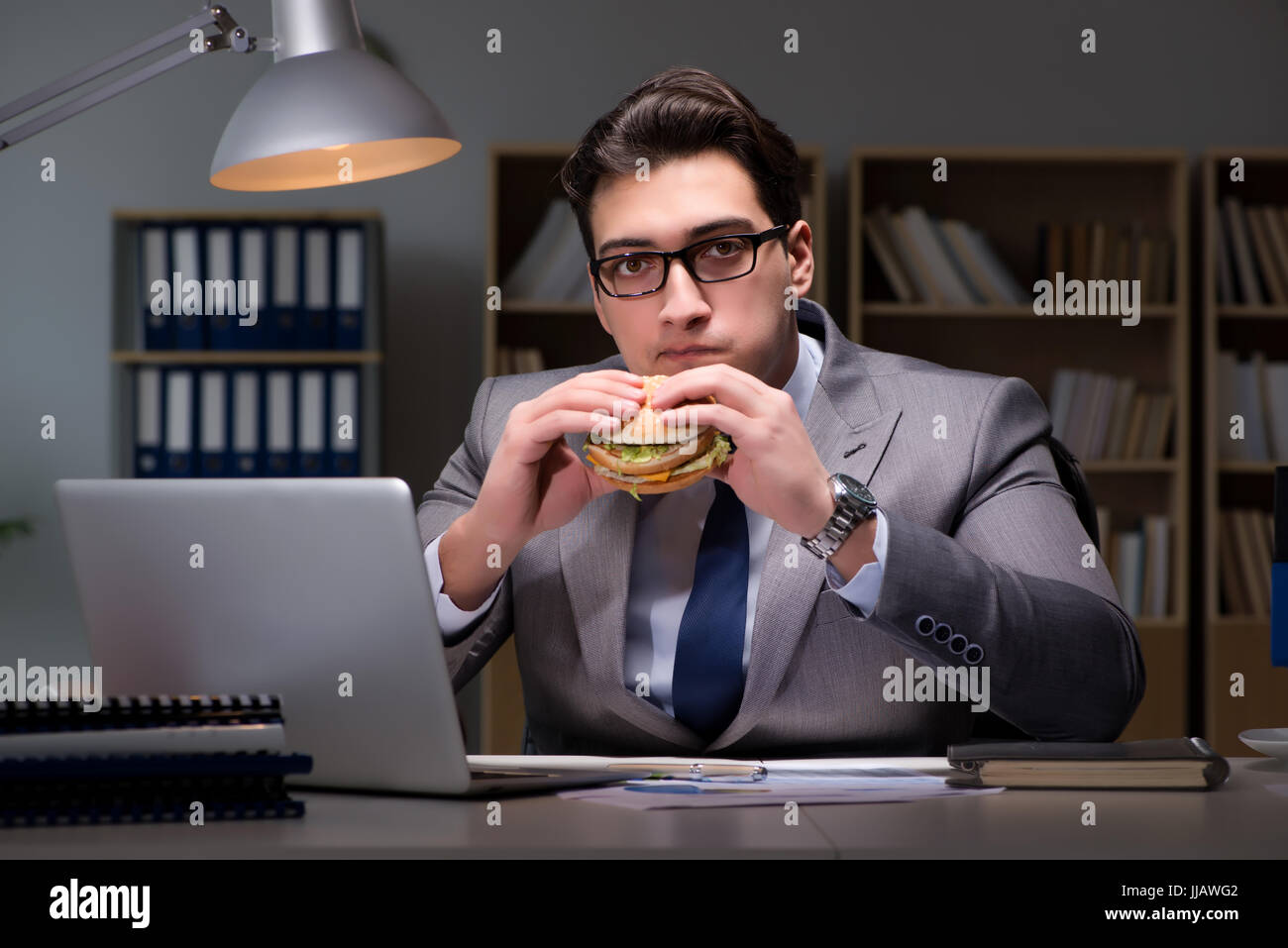 Businessman late at night eating a burger Stock Photo - Alamy