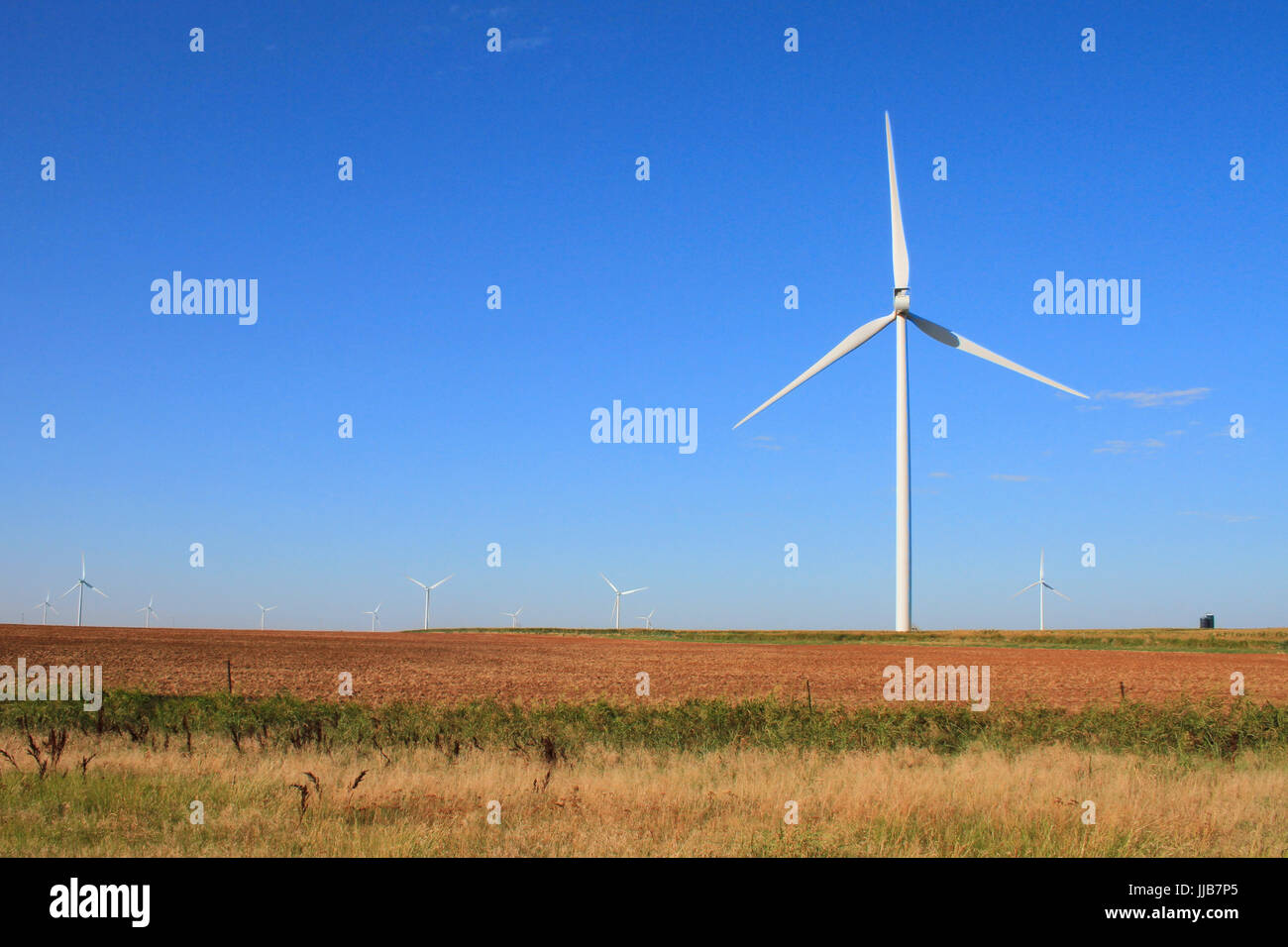 A wind farm in Oklahoma towers over the red soil of an empty crop field ...