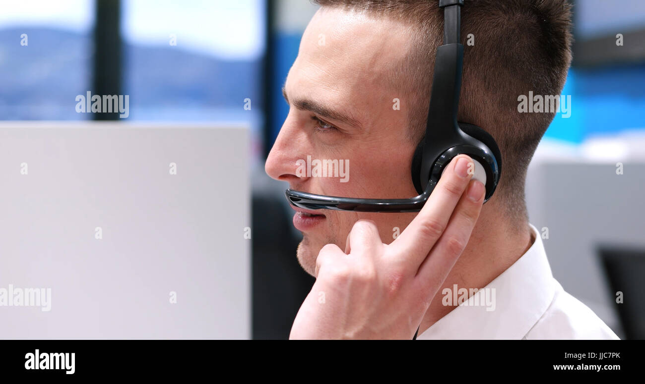 young smiling male call centre operator doing his job with a headset ...