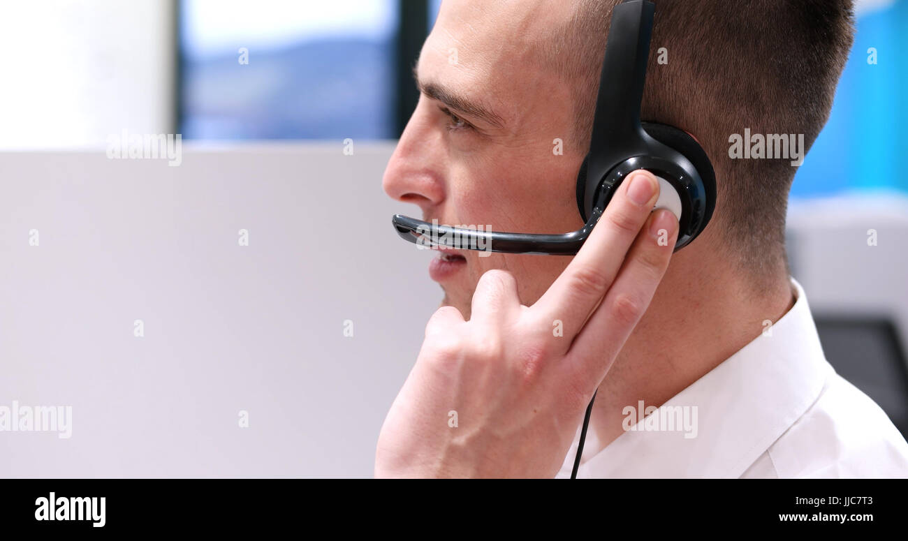 young smiling male call centre operator doing his job with a headset ...