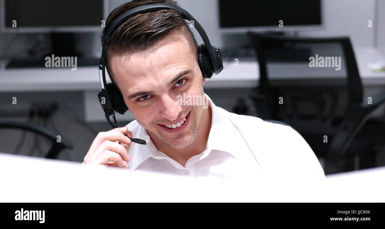 young smiling male call centre operator doing his job with a headset ...