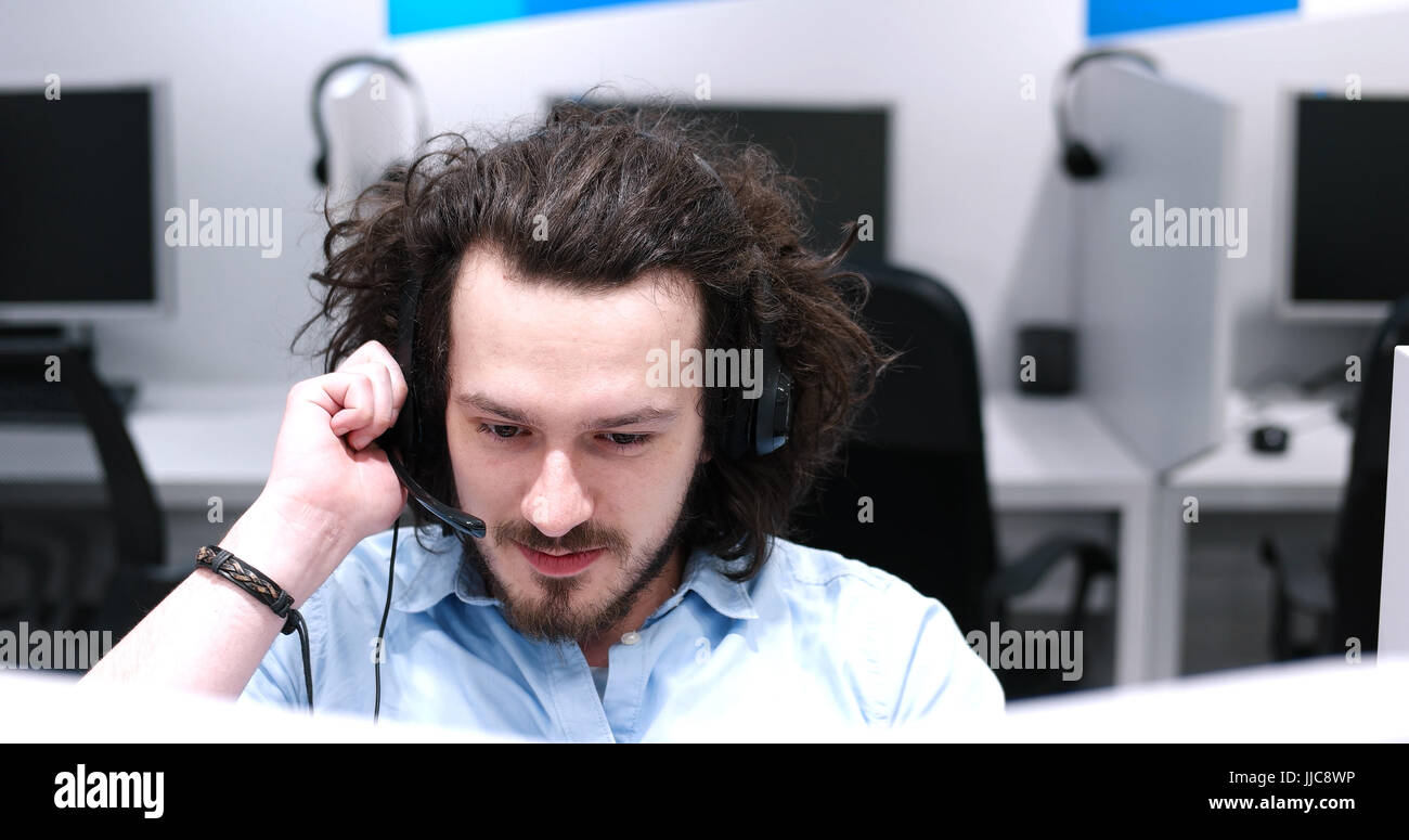 young smiling male call centre operator doing his job with a headset ...