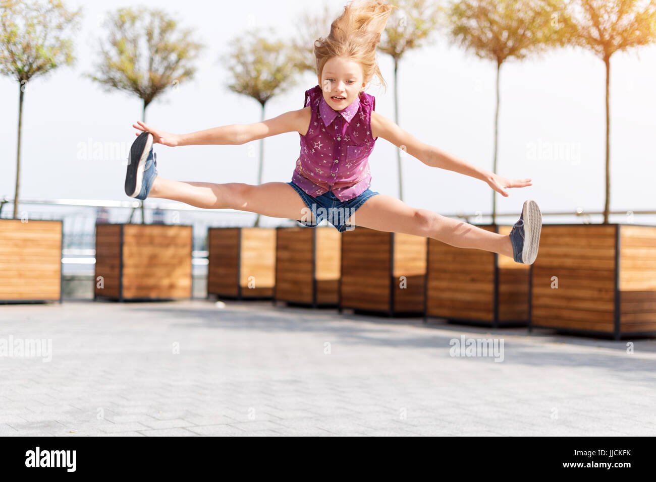 Active kid girl gymnast jumping on the street, doing splits. Stretching ...
