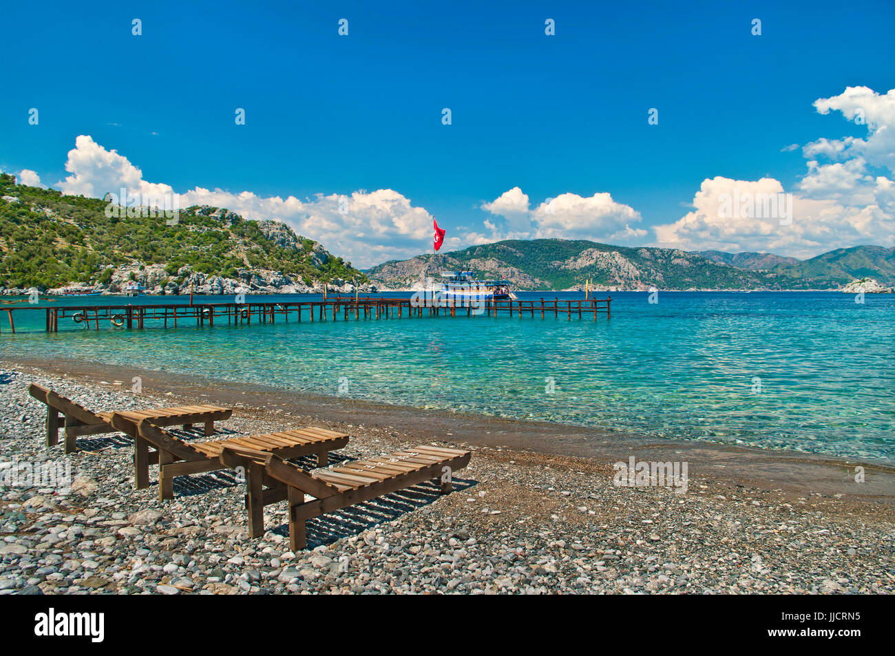 three wooden sunbeds at pebble beach in Amos Bay in Aegean sea with ...