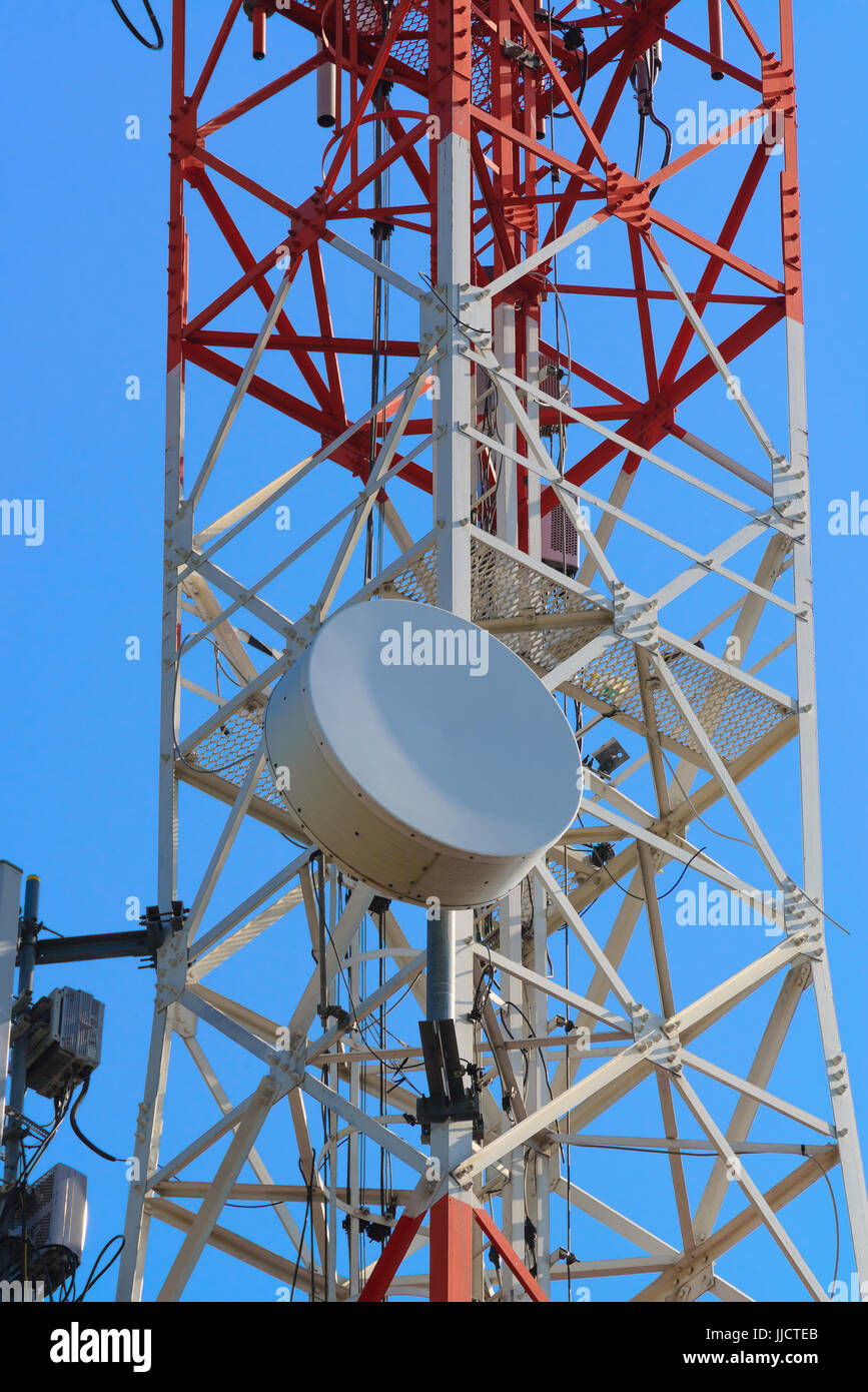 Mobile phone communication antenna tower with satellite dish on blue sky background ...