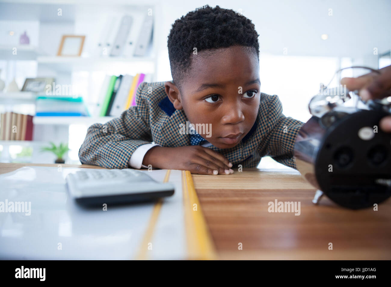 Bored businessman checking alarm clock while leaning on desk at office ...