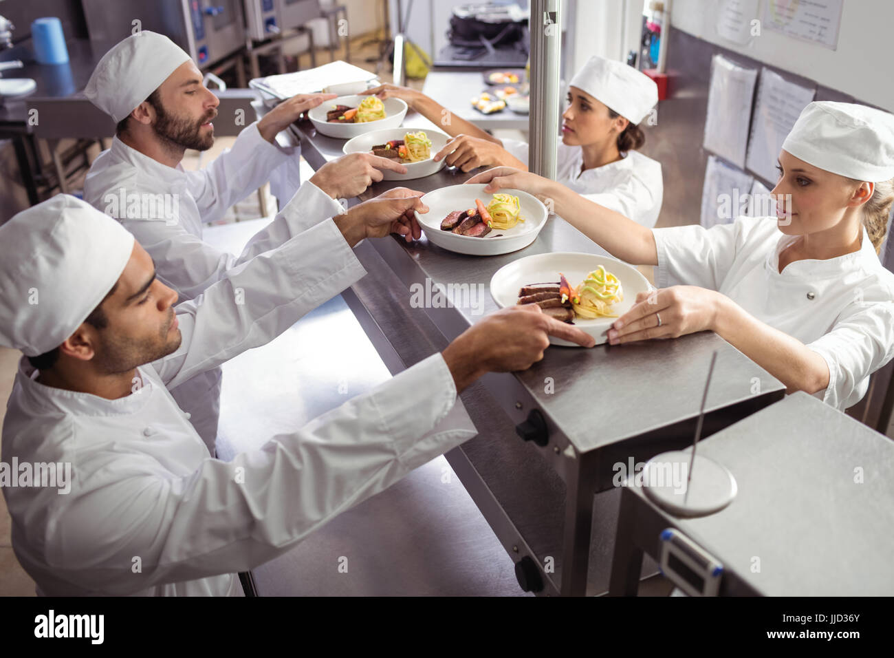Chefs passing ready food to waiter at order station in commercial ...