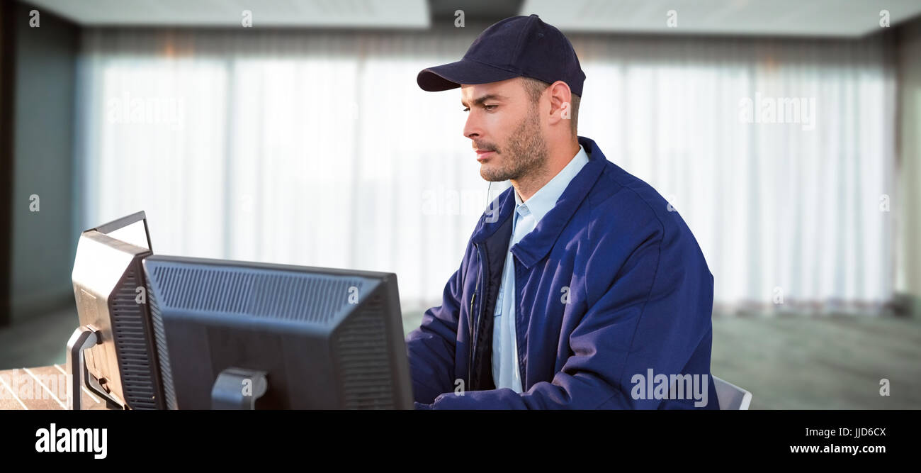 Serious security officer using computer against spacious room with ...