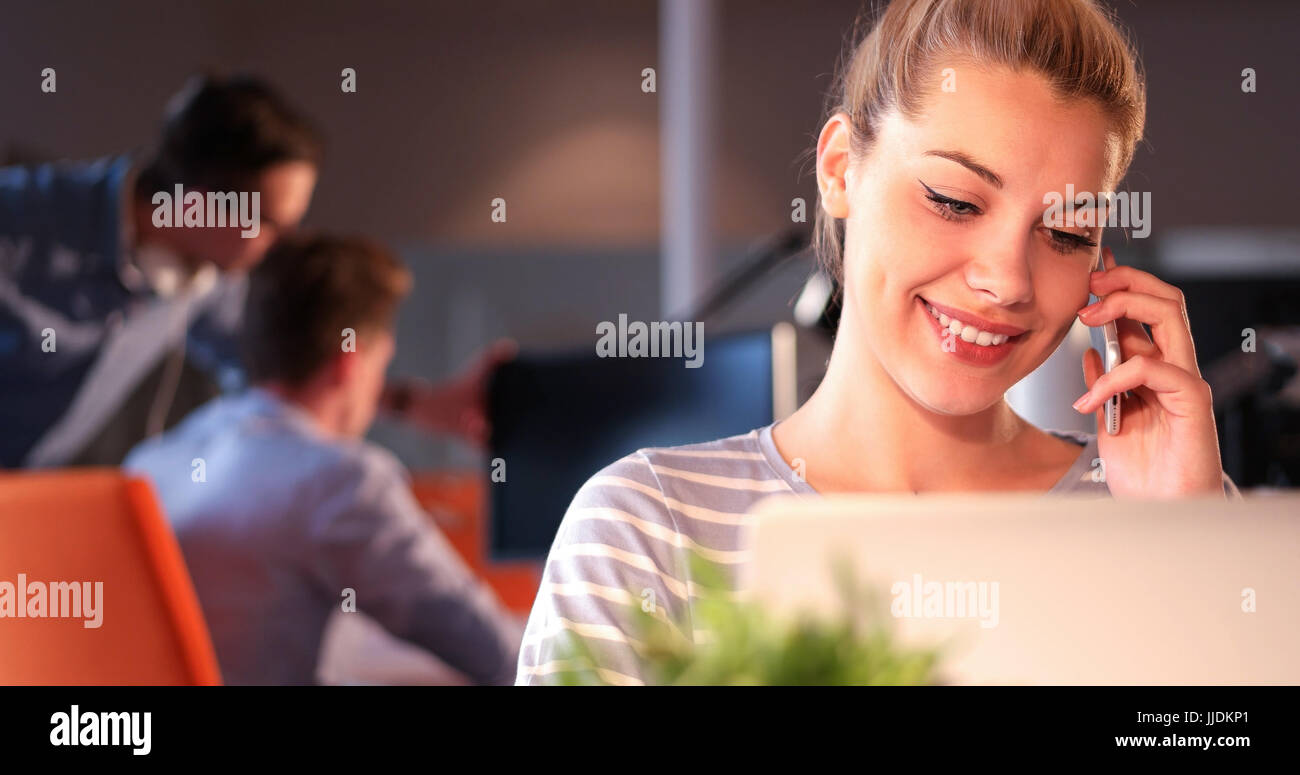 Young woman using mobile phone while working on computer at night in ...