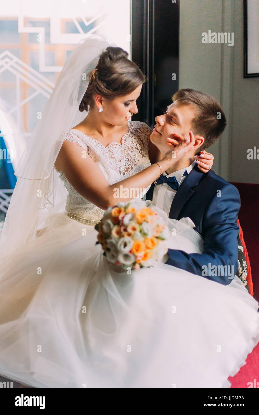 Charming young bride sitting on knees of her loving groom in a ...
