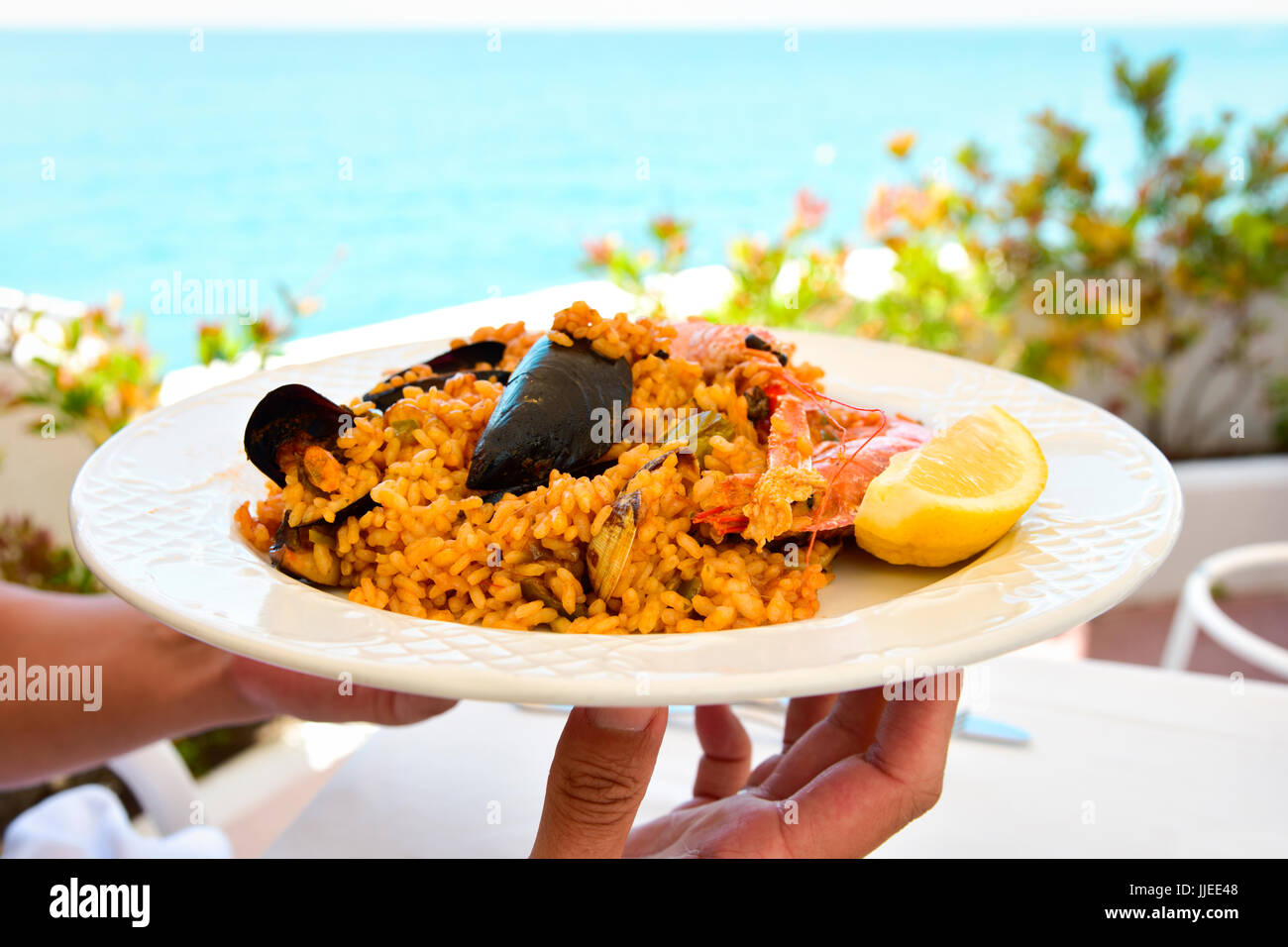 closeup of a young man bringing a plate of typical spanish paella, with ...
