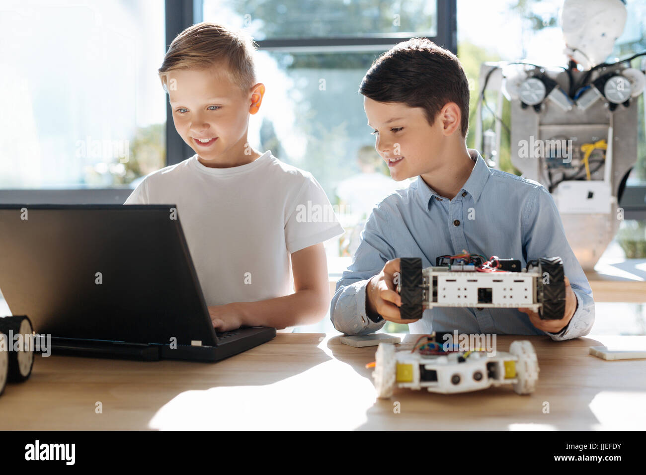 Joyful kid watching his friend program a robotic vehicle Stock Photo ...