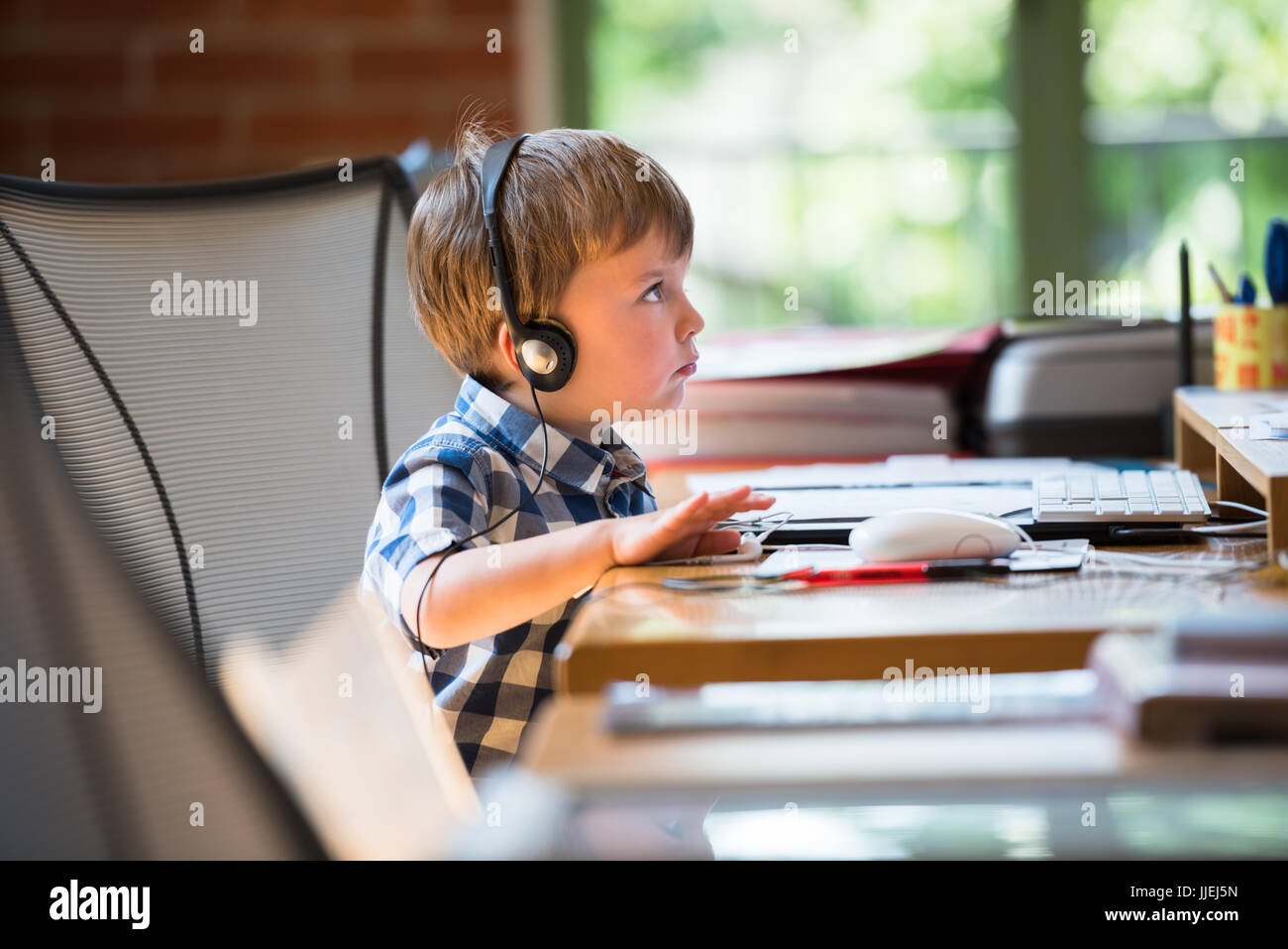 A schoolboy boy studies at home and does school homework listening to ...