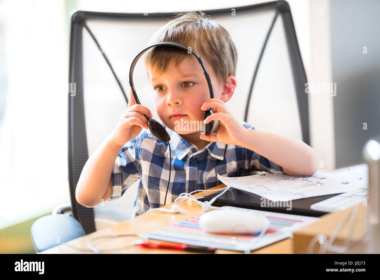 A schoolboy boy studies at home and does school homework listening to ...