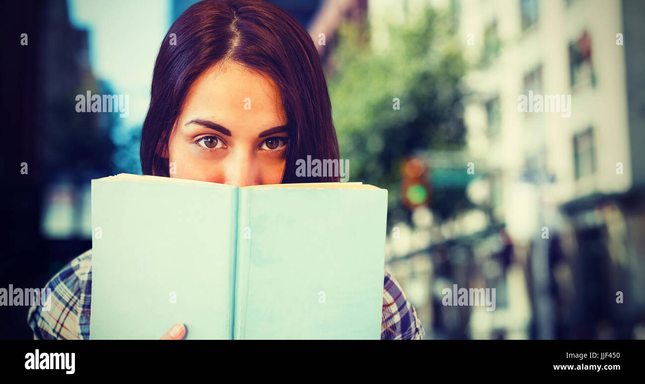 Close up portrait of woman hiding behind book against blur view of a ...