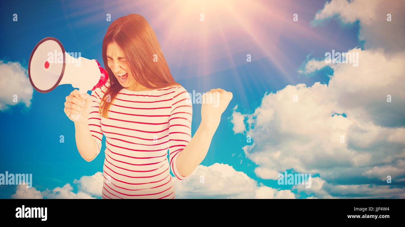 Excited young woman shouting with megaphone against scenic view of blue ...