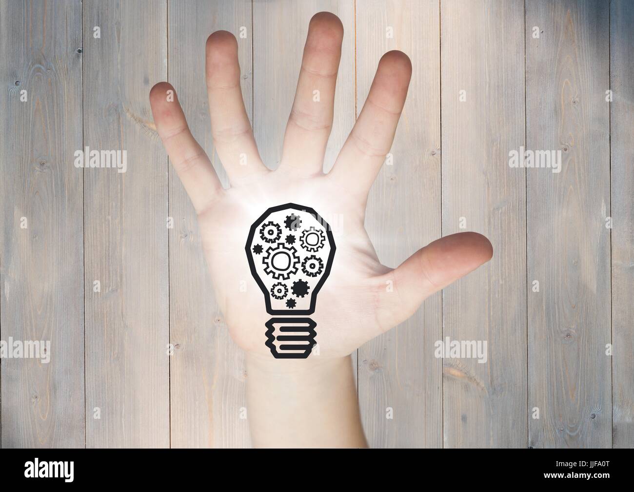 Digital composite of Hand with cogs in lightbulb graphic and flare in ...