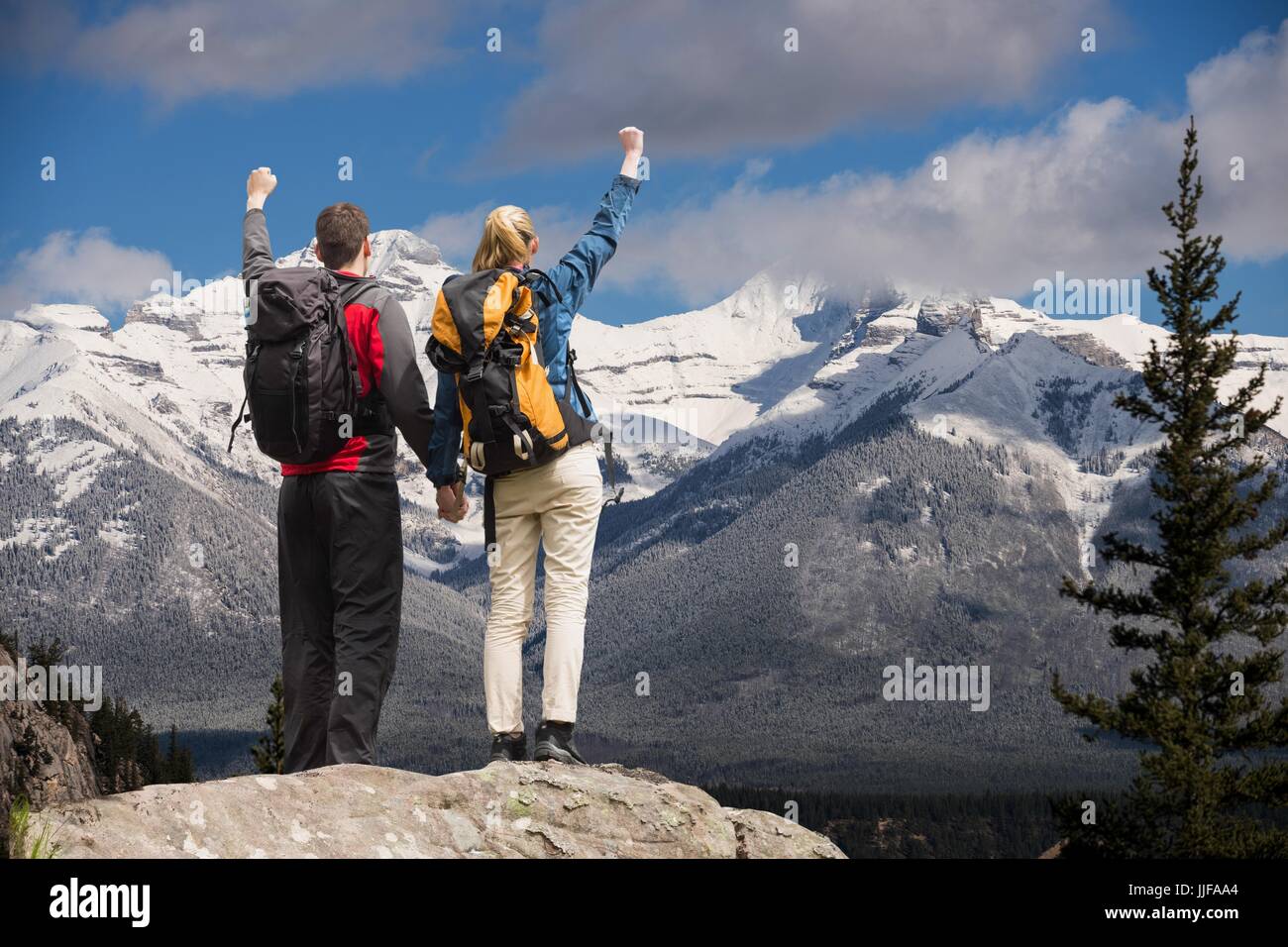 Digital composite of Couple raising their hands on the top of mountains ...