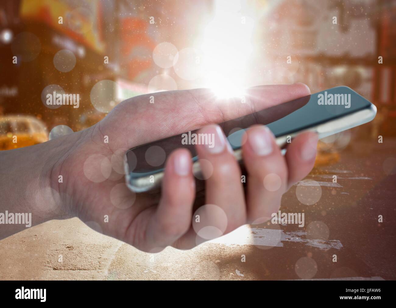 Digital composite of Hand with phone against blurry street with bokeh ...