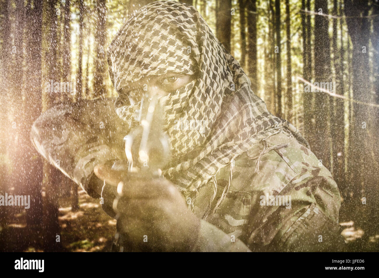 Portrait of face covered soldier aiming with rifle against trees in a ...