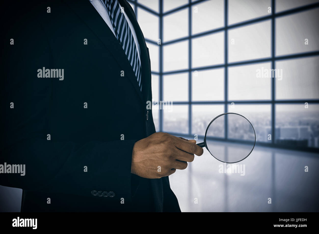 Mid section of businessman holding magnifying glass against room with ...