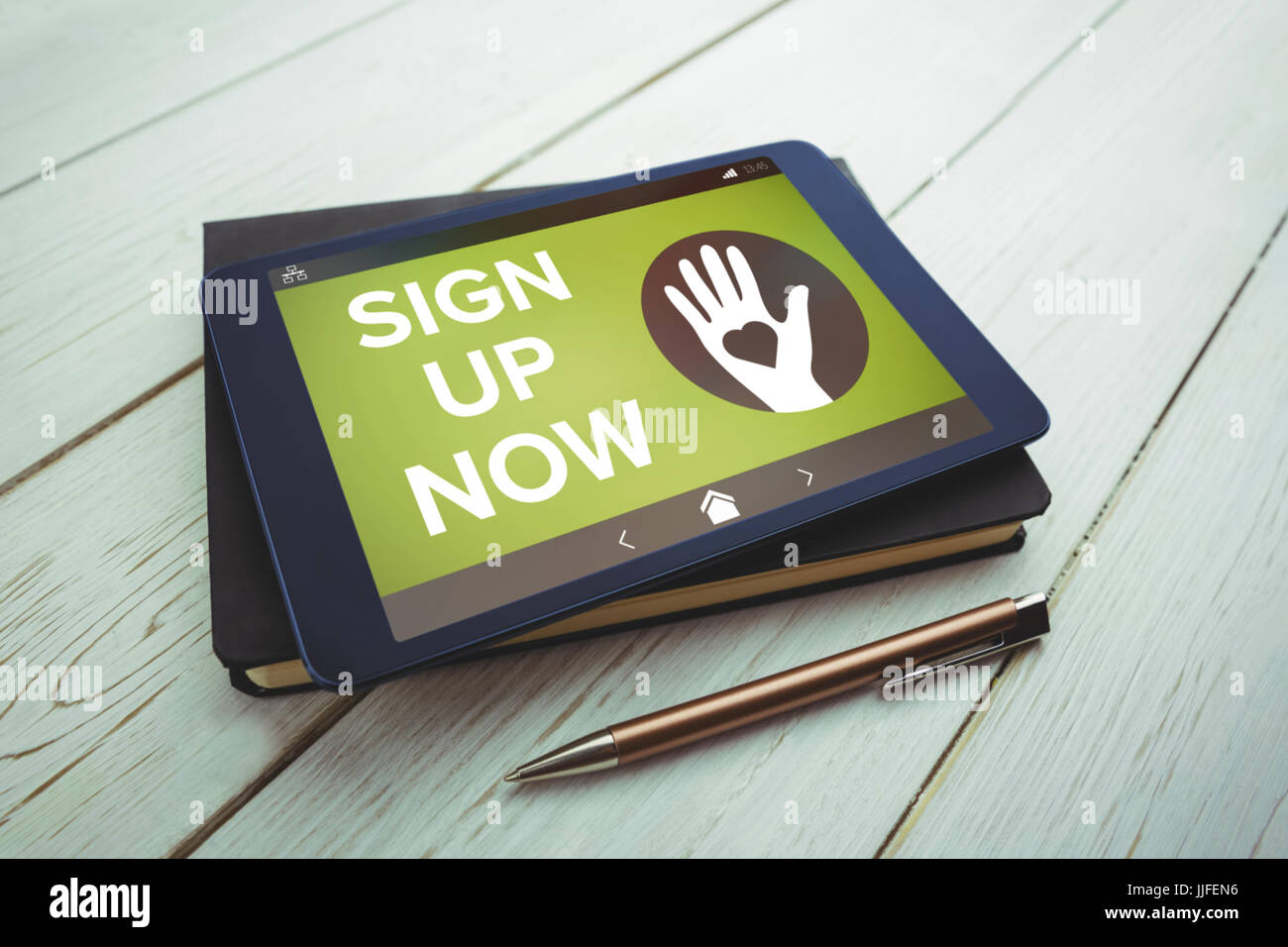 Sign Up Now text with icons on green screen against tablet and pen on ...