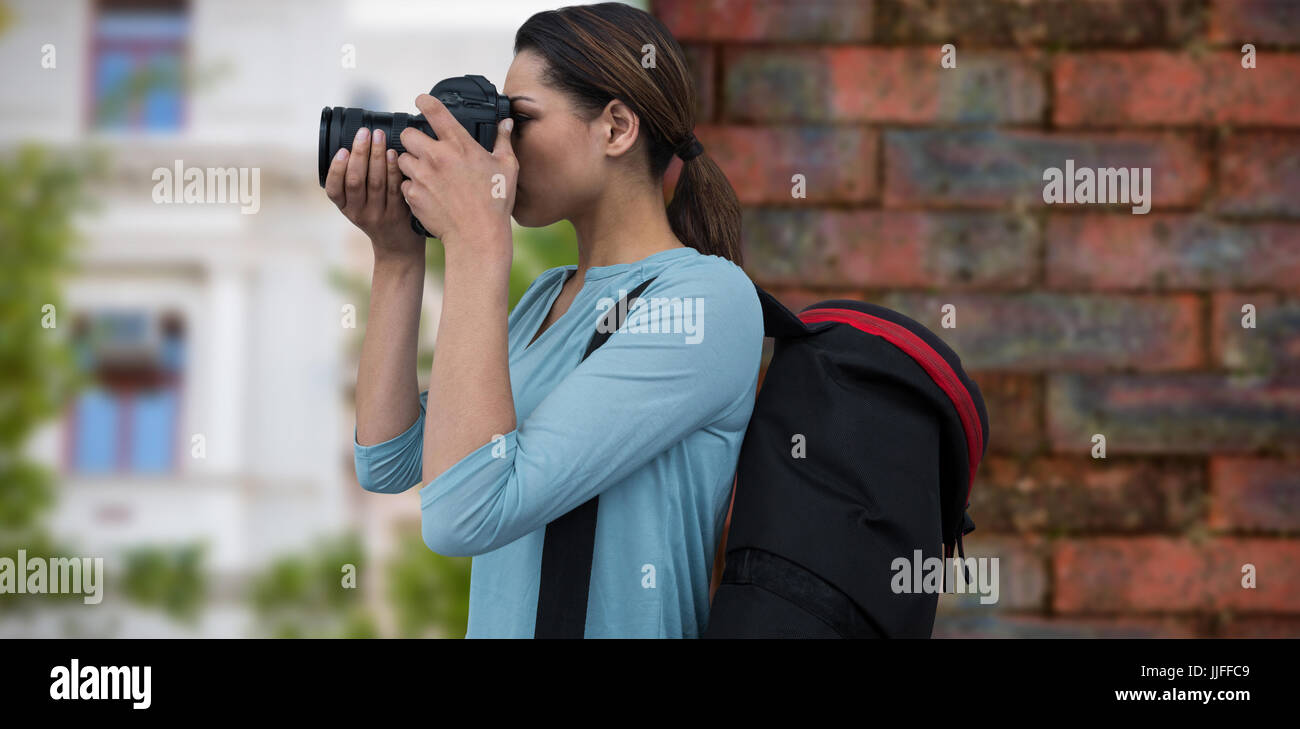 Side view of woman photographing through digital camera against wall of ...