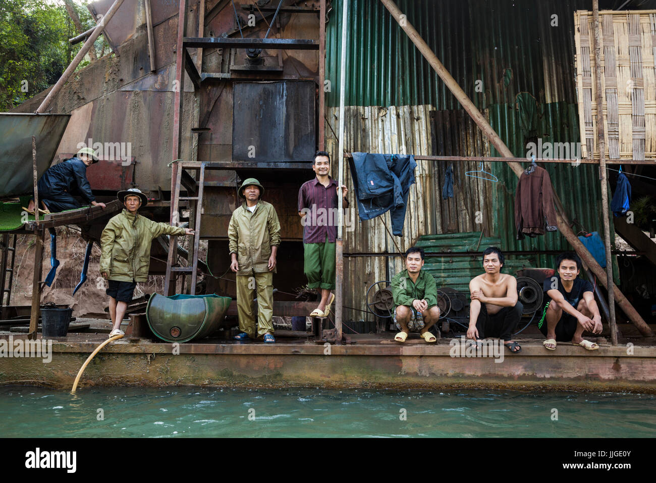 Vietnamese and Lao men stand on the deck of a mechanical gold dredge ...