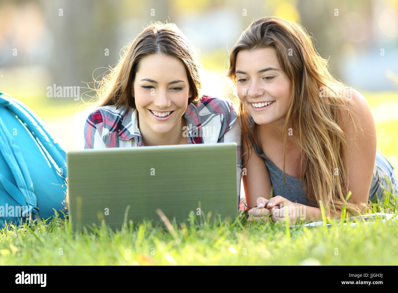 Front view of two happy students watching on line content with laptop ...